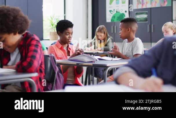 Diverse female teacher and happy schoolchildren at desks learning sign ...