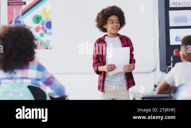 Diverse female teacher and happy schoolchildren at desks reciting in ...