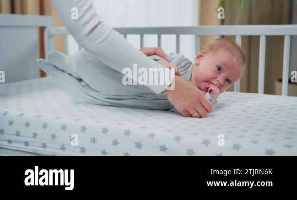 Baby boy first turning over on stomach in white crib with mothers help ...