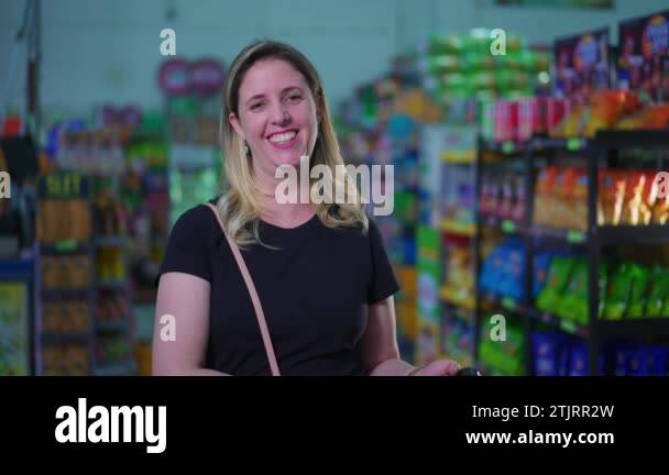 Joyful female consumer standing inside supermarket store smiling at ...