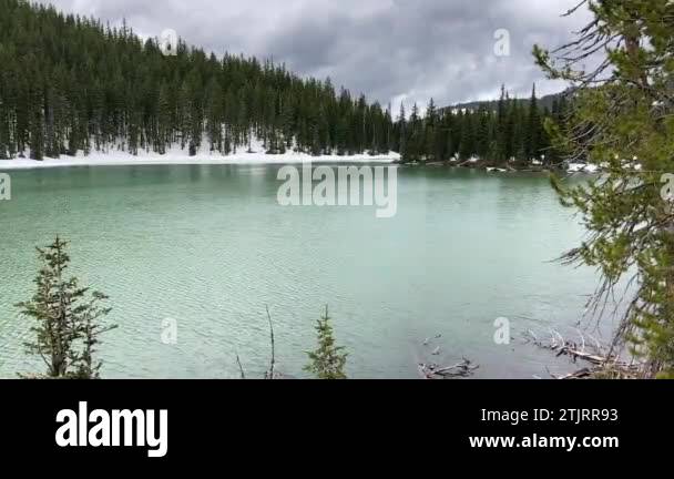 The beautiful aqua Devils Lake, surrounded by evergreen trees and snowy ...