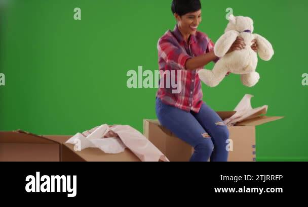 Cute black female unpacking box in new home, excited to find teddy bear ...