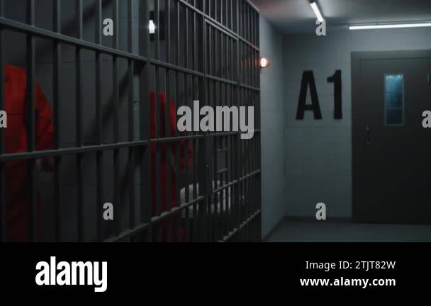 Prisoners in orange uniforms walk in prison cells, hold metal bars ...