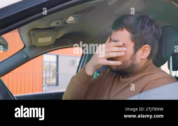 An exhausted and exhausted young man sits in the drivers seat in the ...