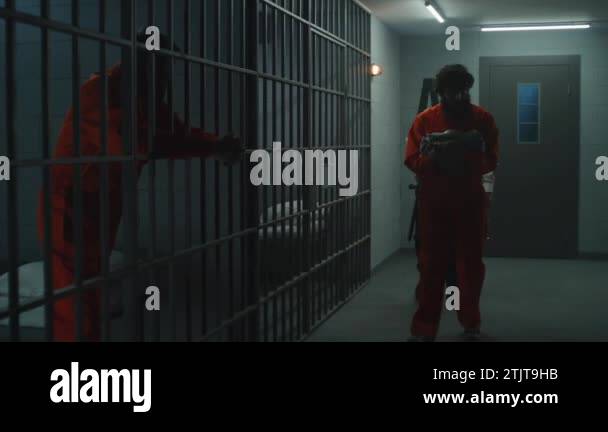Prison officer locks criminal in orange uniform in jail cell. Depressed ...