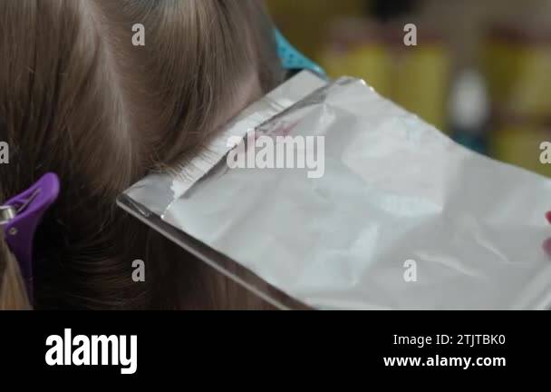 Masters hands fold strands of female hair in special sheet of foil ...