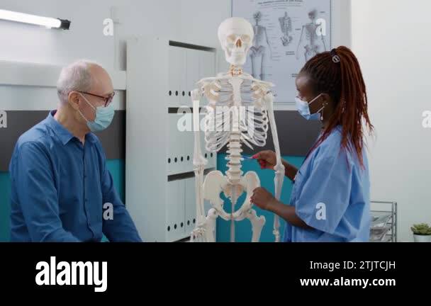 Female nurse analyzing human skeleton bones with old man, explaining ...