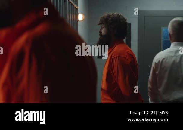 Two prisoners in orange uniforms stand facing the metal bars in front ...