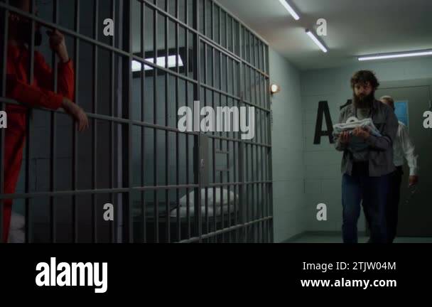 Prison guard leads male criminal to jail cell. Depressed prisoner leans ...