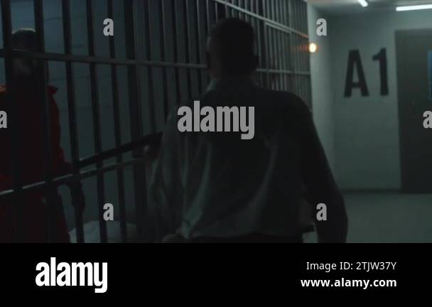 Jailer with police baton watches criminals in prison cells. Prisoners ...