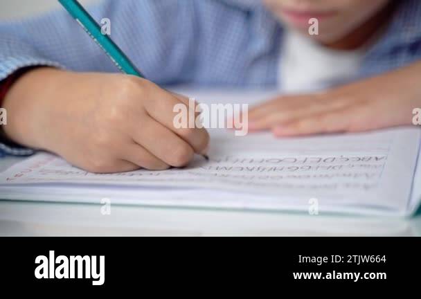 Elementary school student boy or girl writing letters, studying at desk ...
