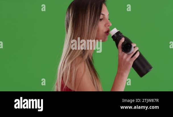 Close up side view of millennial woman in red drinking water from ...