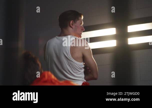 Prisoner stands in prison cell with barred window, talks to cellmate ...