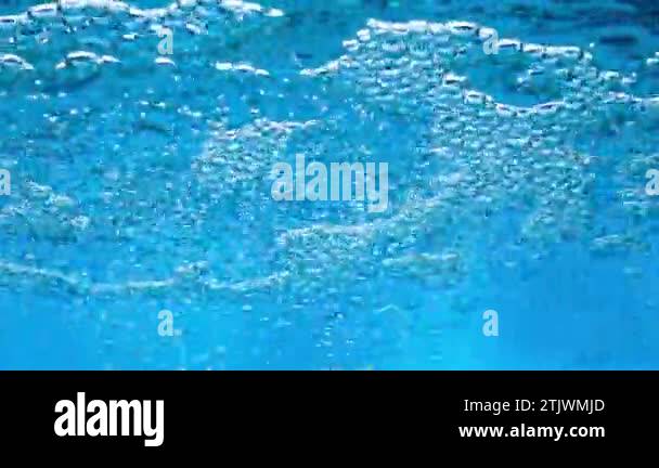 A stream of air bubbles rising onto the surface of blue water from the ...