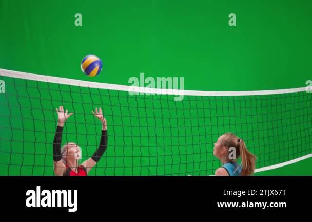 Two young women in blue and red uniforms playing volleyball on green ...
