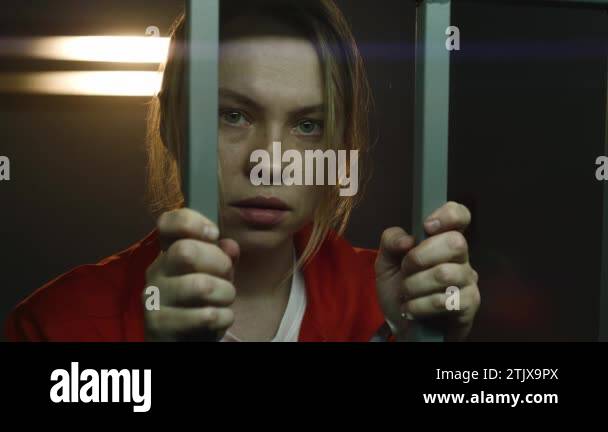 Scared female prisoner in orange uniform holds metal bars, stands in ...