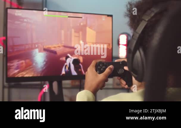 Rear view of zoomer boy in headphones using controller while playing ...