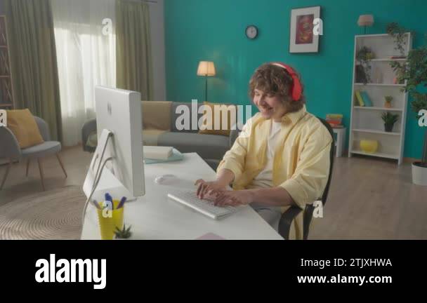 A young guy in red wireless headphones sits at a computer. The man ...