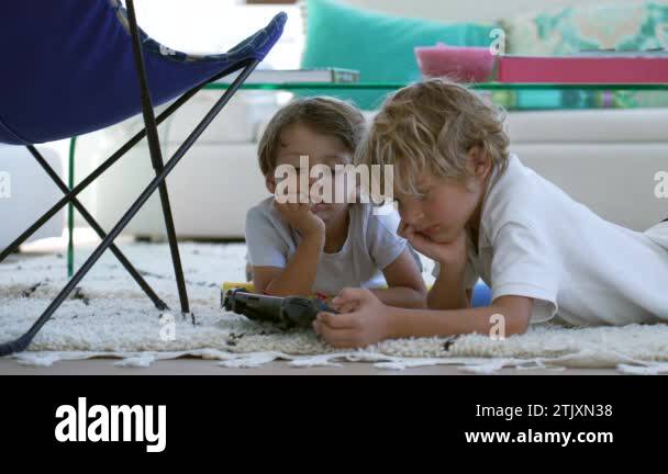 Two small boys watching media content online lying on living room floor. Candid brothers looking ...