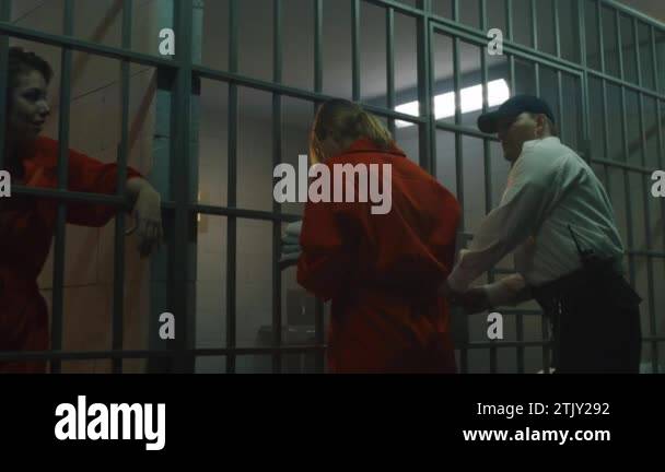 Prison employee leads female prisoner in orange uniform to prison cell ...