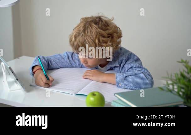 Elementary school student boy or girl writing letters, studying at desk ...