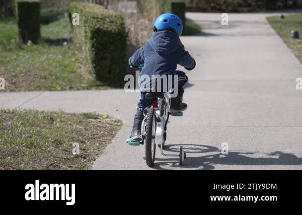 Back of child riding bicycle outdoors wearing helmet. One little boy ...