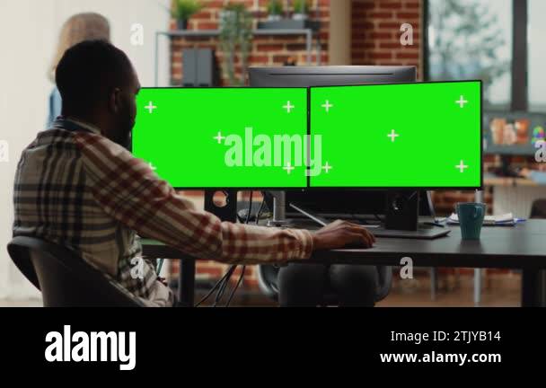 African american man analyzing greenscreen on multi monitors, working ...