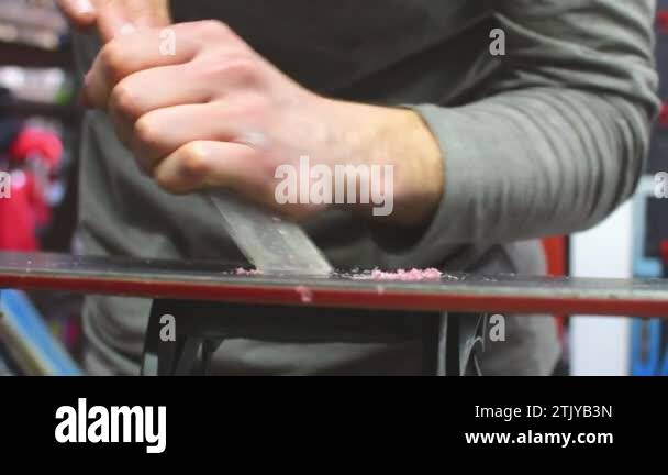 Repairman scrape wax off from snowboard with scraper in repair shop ski ...