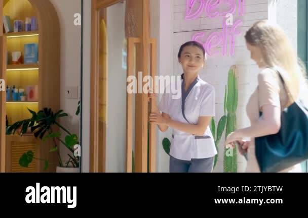 Back view of young female client entering spa salon, admin opens door ...