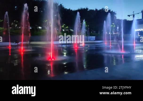 Pedestrian ground fountain illuminated by colorful lights at night. Big ...