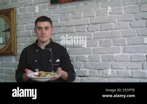 Chef in black uniform presents taste salad on white brick wall ...
