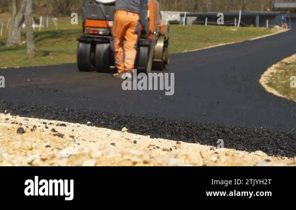 Road workers levelling and smoothing freshly laid asphalt surface on ...
