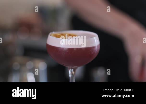 A bartender in an expensive edith hotel pours a prepared pink cocktail from a shaker into a ...