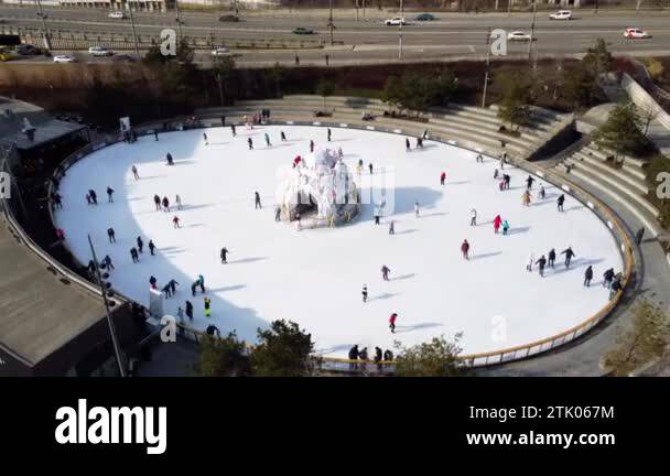 Ice skating rink in open air in city on sunny winter day. Many people ...