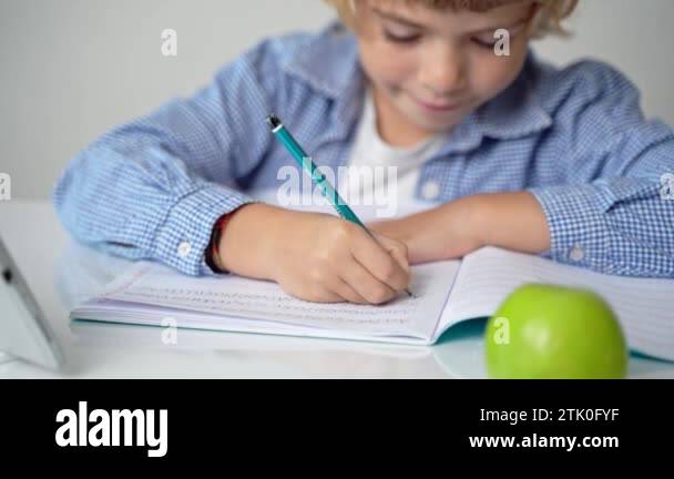 Elementary school student boy or girl writing letters, studying at desk ...