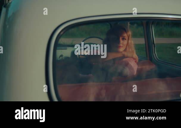 Blonde girl in pink vintage dress sits behind the wheel of a retro car ...
