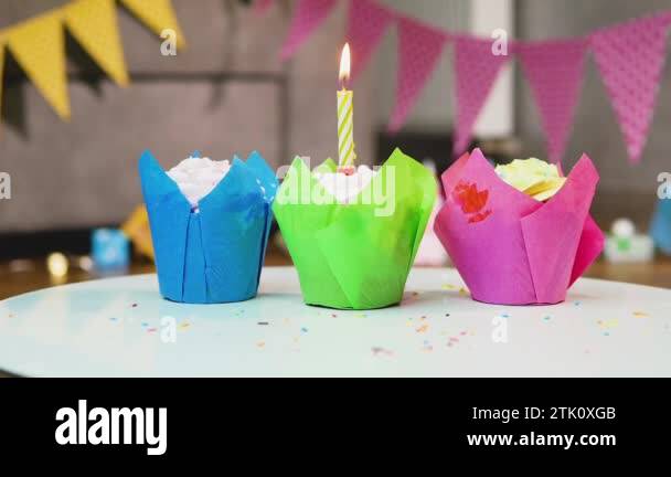 Close-up of multi-colored festive muffins with a burning candle and ...