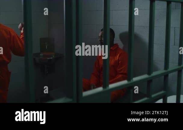 Two African American prisoners in orange uniforms talk. One man sits on ...