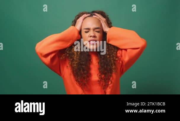 Frustrated and angry young woman tears hair out - green studio ...