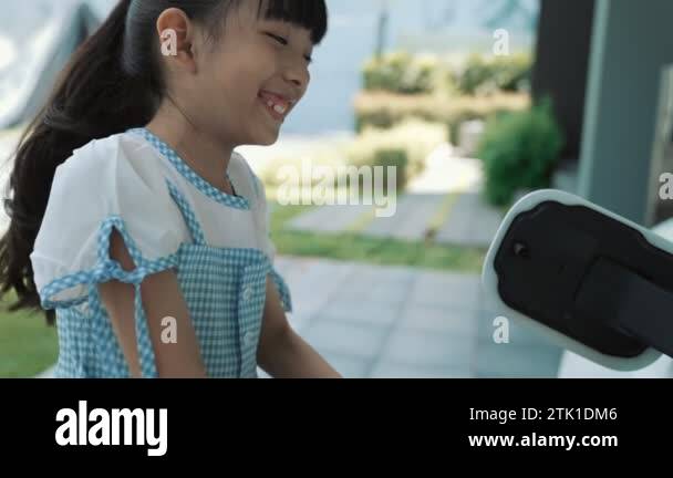A playful girl holding an EV plug, a home charging station providing a ...