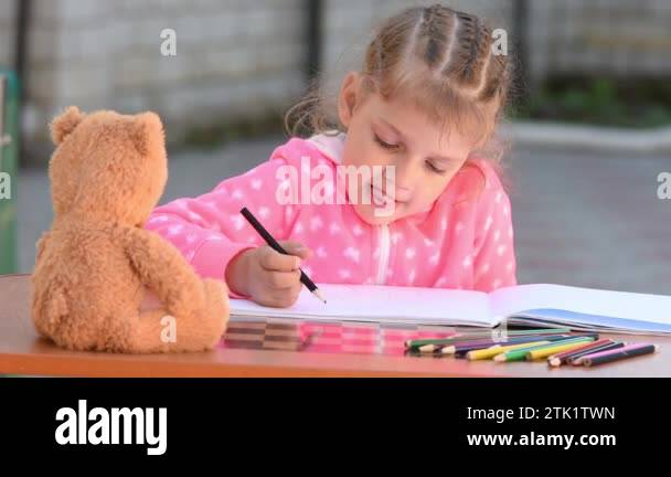 Five-year girl with enthusiasm draws a teddy bear sitting in front of ...