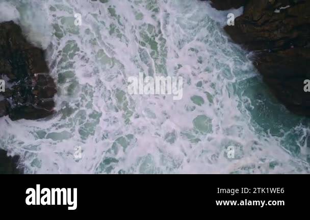 Foamy ocean water bubbling between coastal dark rocks in super slow ...