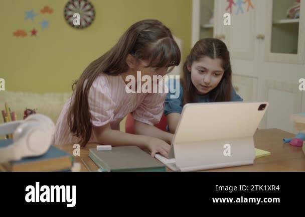 Smart elementary school girls doing math homework with tablet computer ...