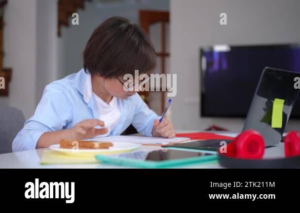 Concentrated smart schoolboy eating snack doing homework writing with ...