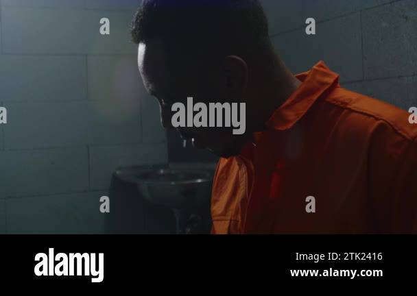African American prisoner in orange uniform reads Bible in prison cell ...