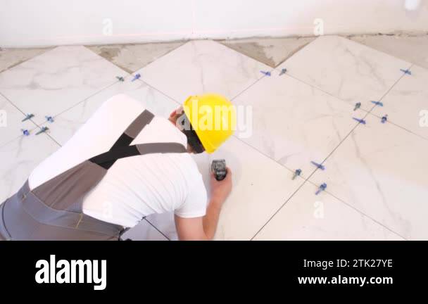 A professional builder installs ceramic tiles in a new building. Tiler ...