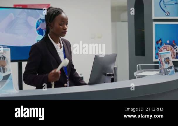 Young receptionist working at clinic reception counter, using landline ...