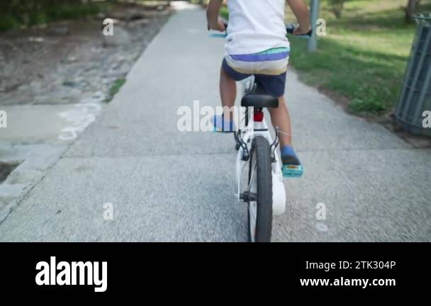 Back of child rides bicycle at park. One active young boy riding bike ...
