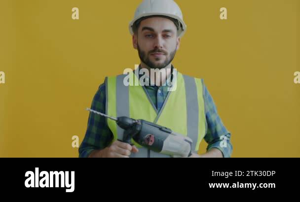 Portrait of playful man in safety uniform holding electric drill then ...