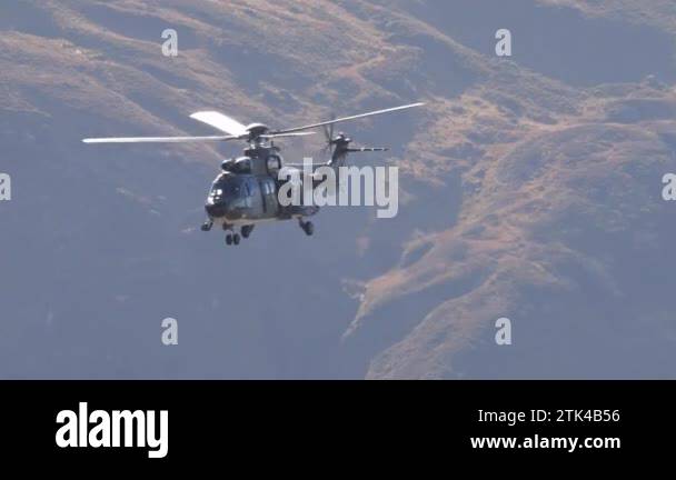 Military helicopter in flight at high speed in a narrow mountain valley ...